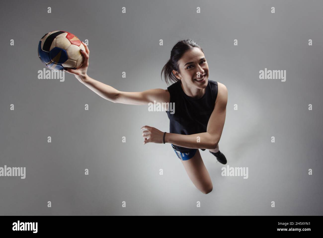 Handball player posing on light gray background. Girl jumping with ball ...