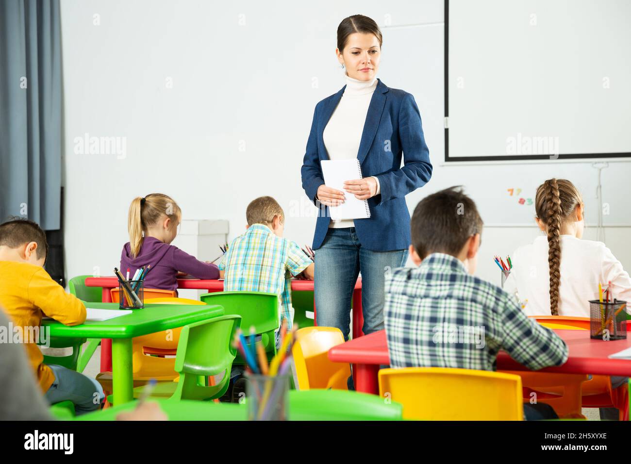 Teacher controlling writing of elementary school students Stock Photo ...
