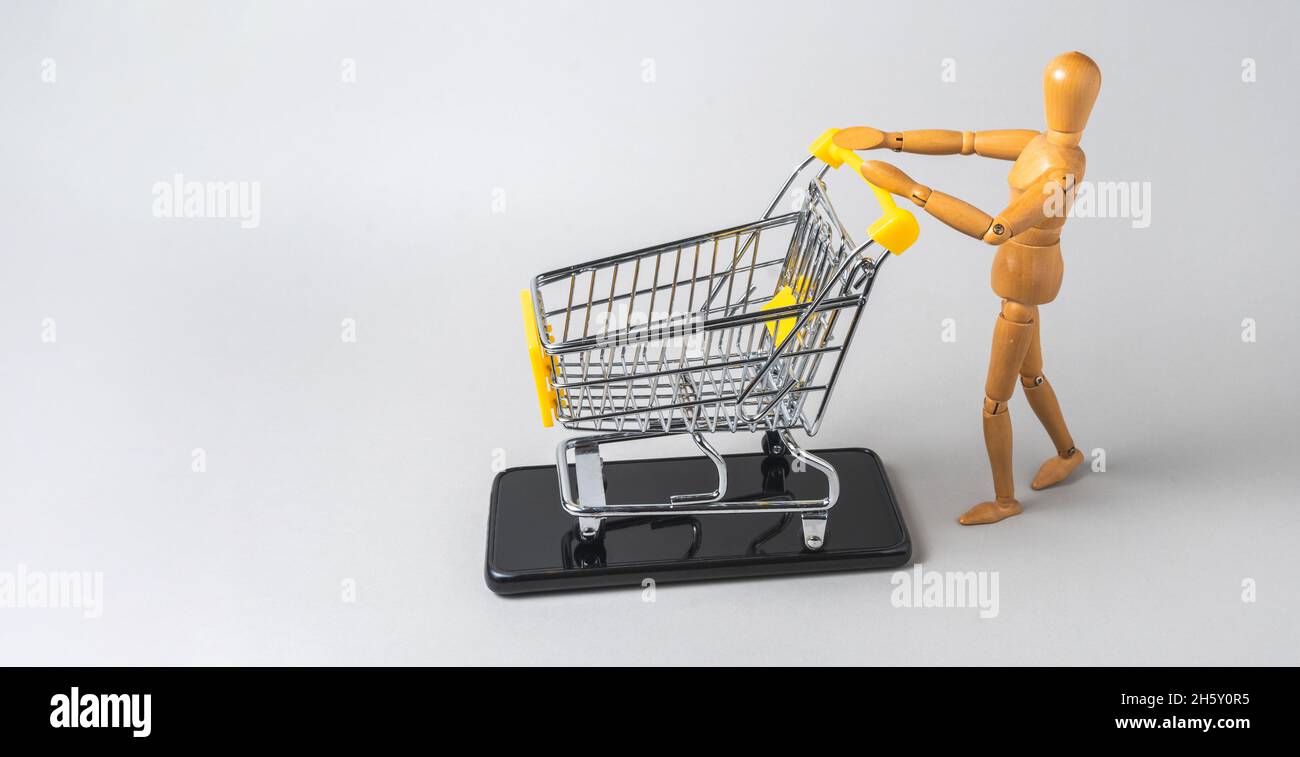 Wooden human figure with a miniature shopping cart on a cell phone ...