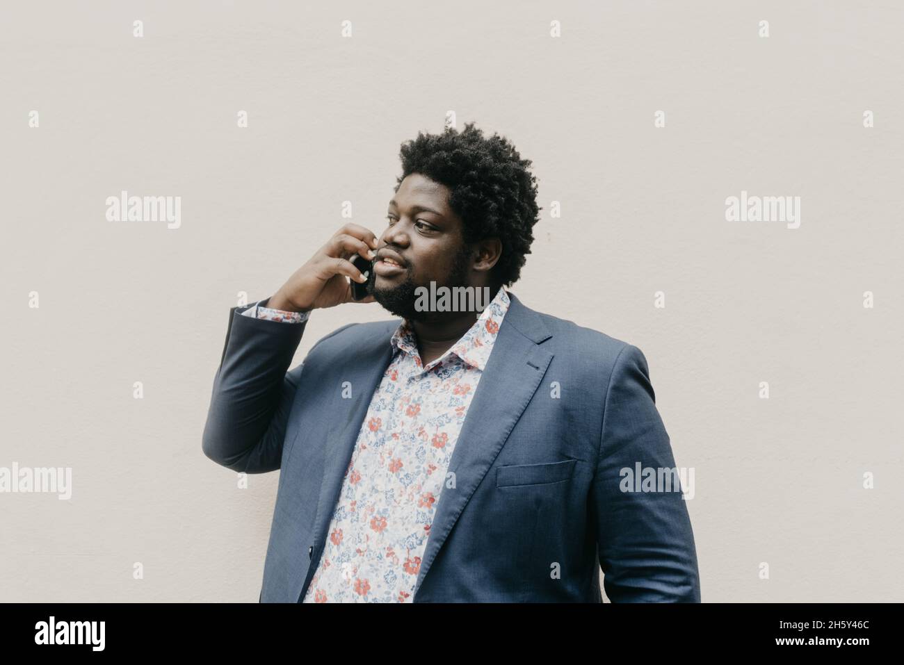 Shallow focus of a black man talking on his phone on a blank wall ...