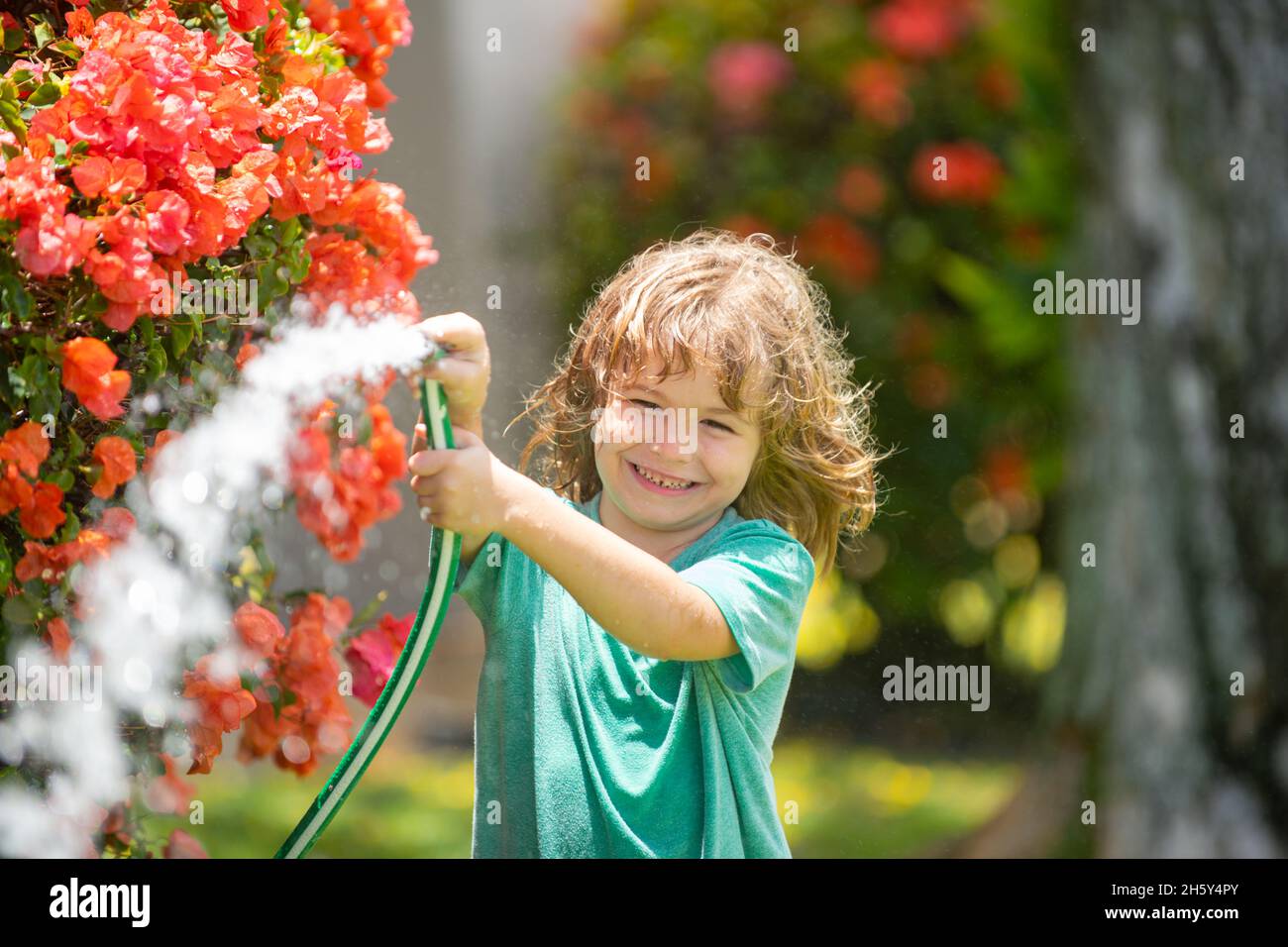 Kid playing in garden, pours from the hose, makes a rain. Happy ...