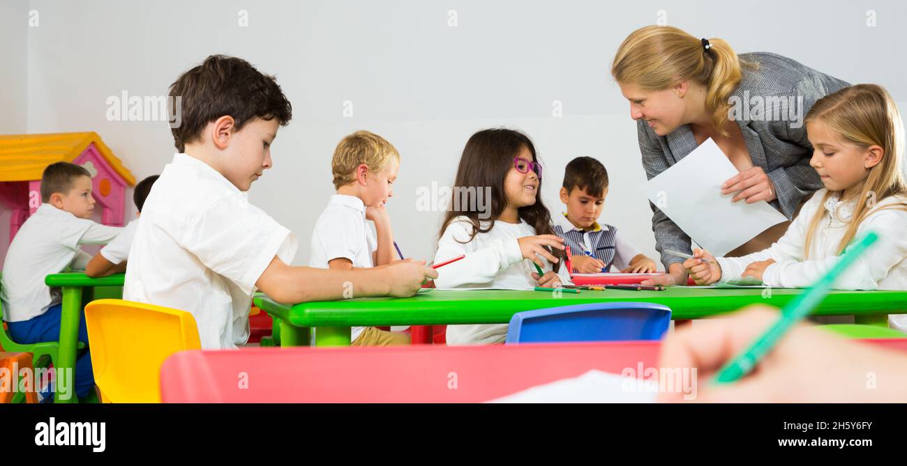 Schoolkids working and teacher helping them Stock Photo - Alamy