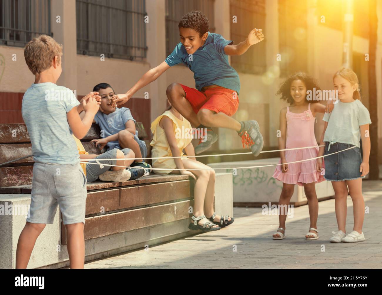 Energetic kids playing and skipping on elastic jumping rope in yard ...