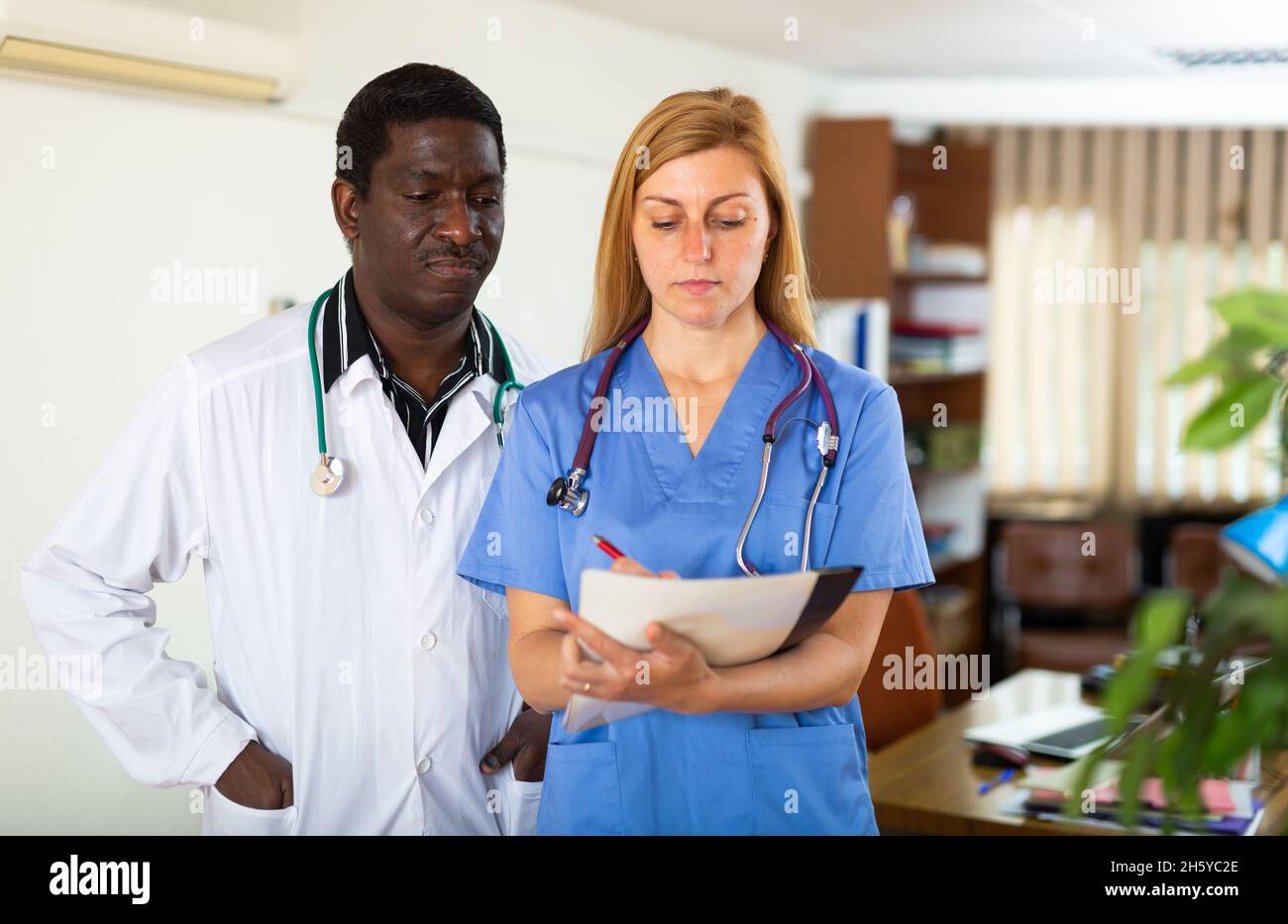 Portrait of two professional qualified health workers in medical office ...
