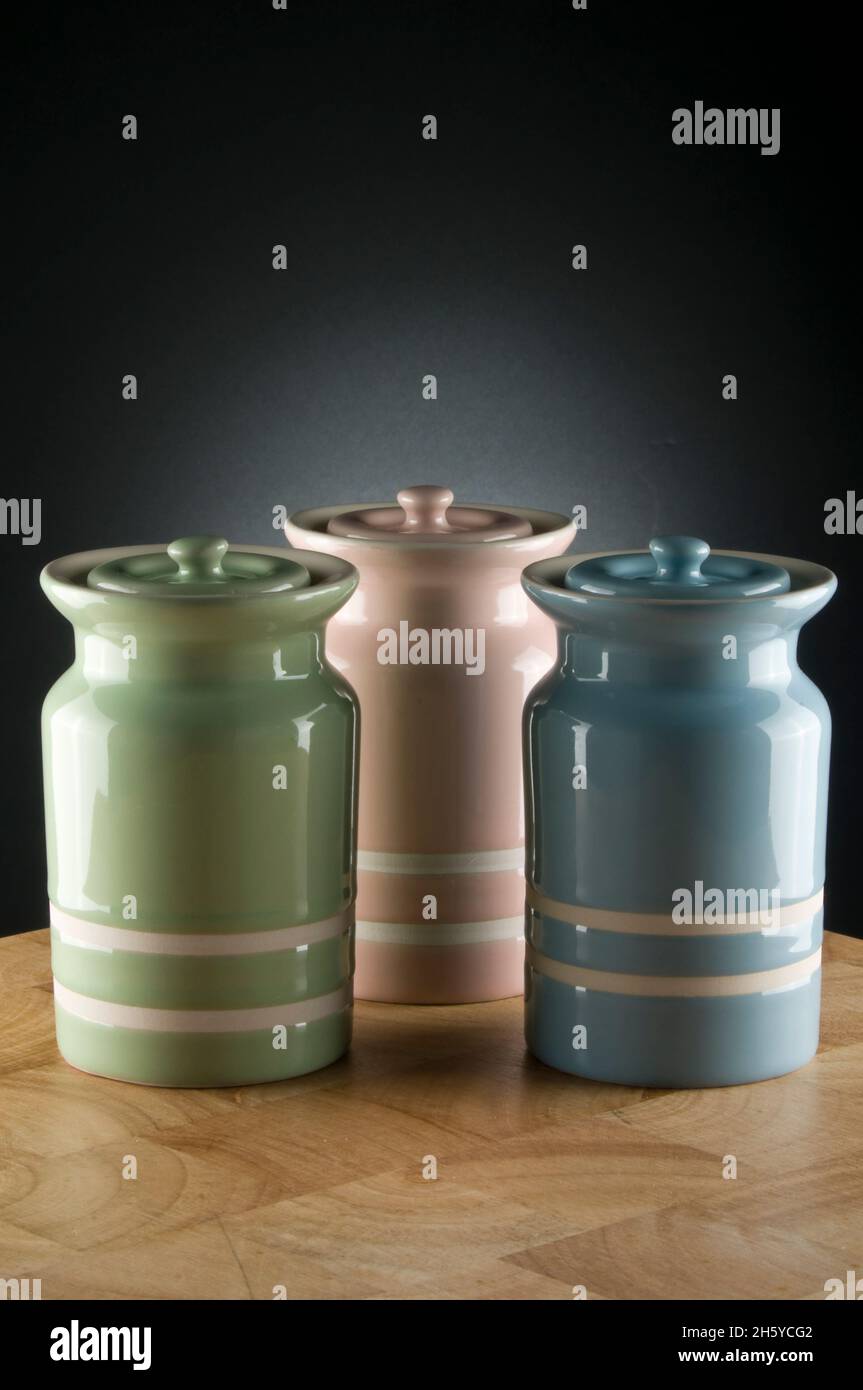 Three colourful ceramic canisters on timber bench with grey spot on ...