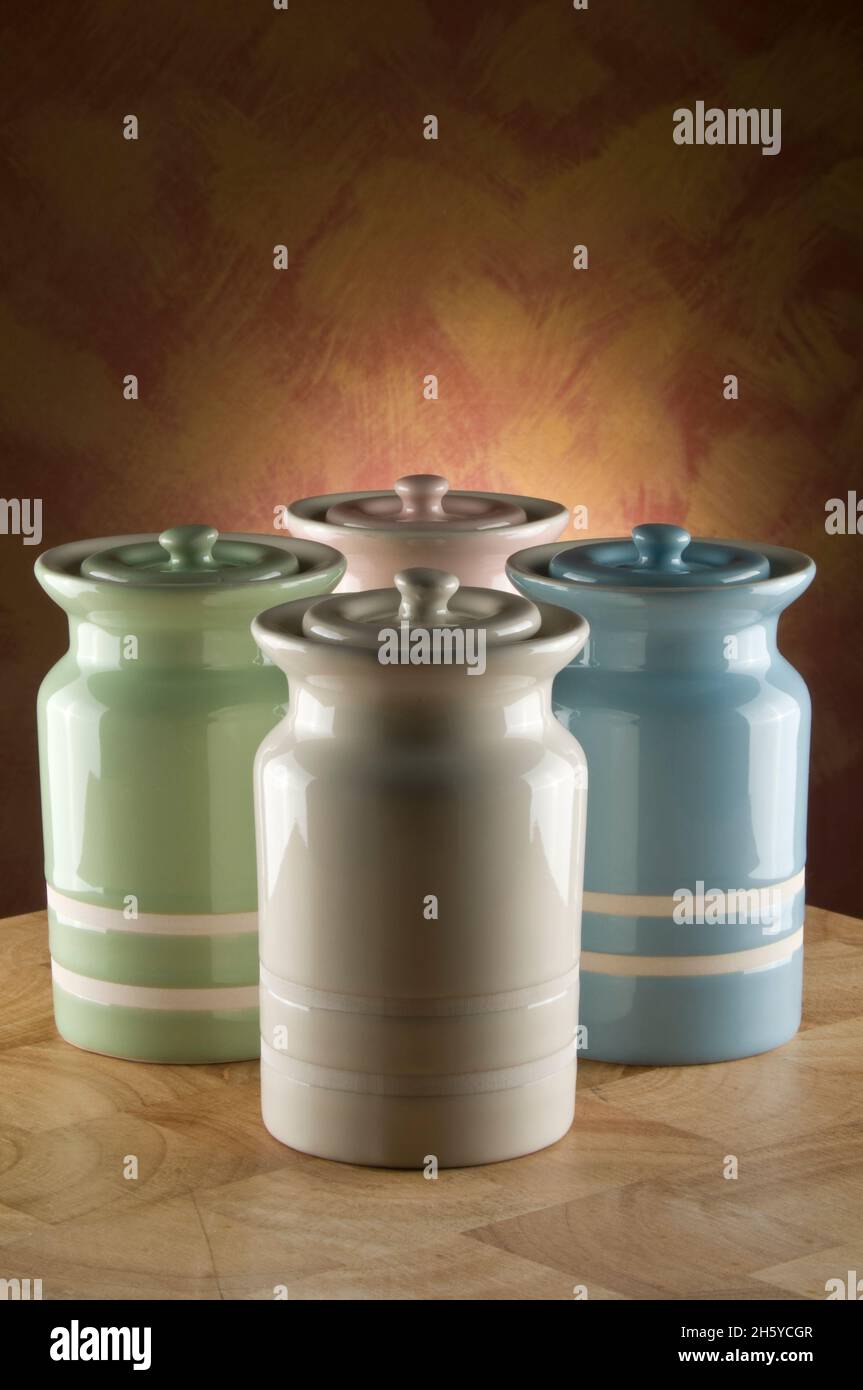 Four colourful ceramic canisters on timber bench with rustic background ...