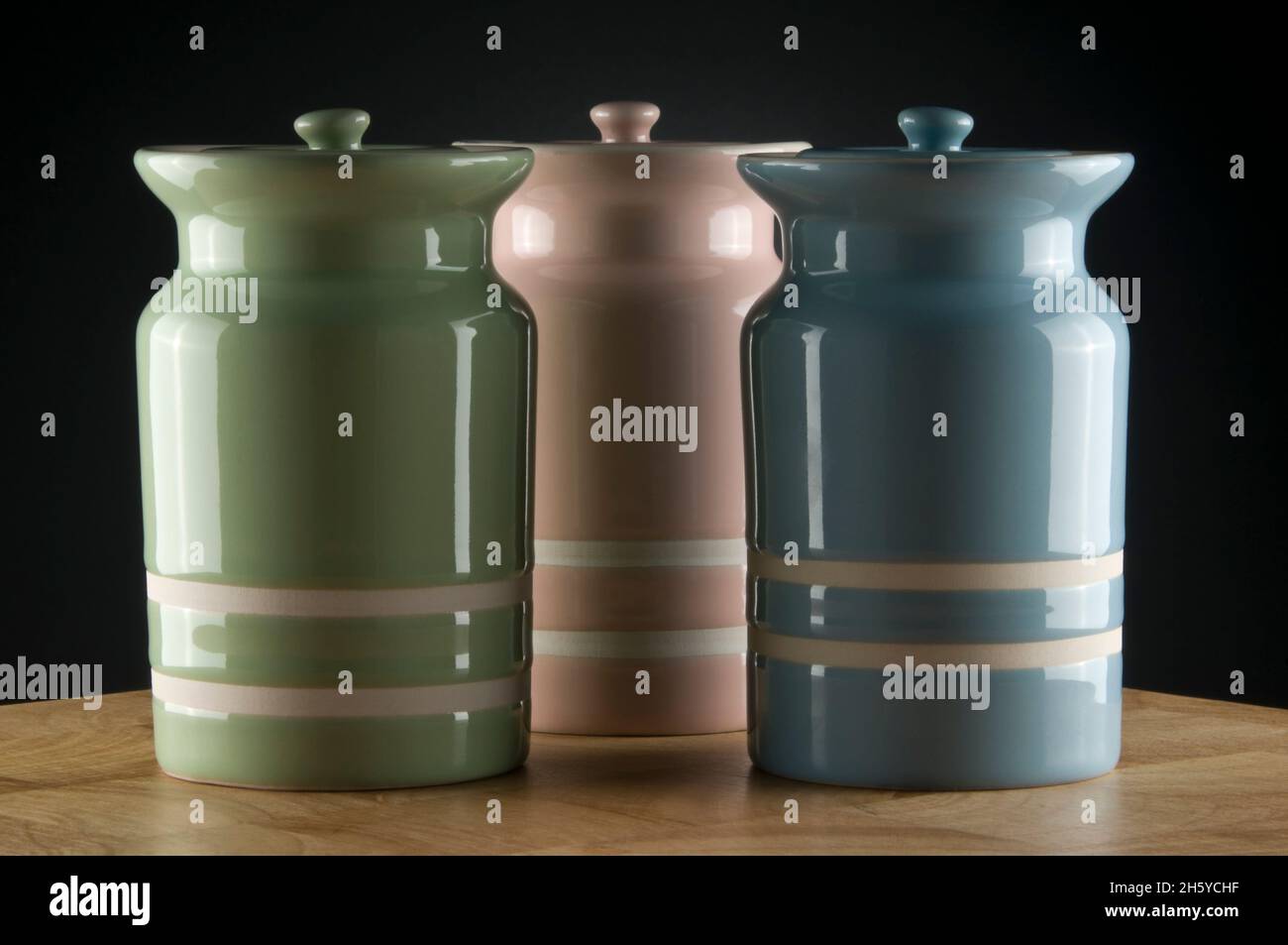 Three colourful ceramic canisters on timber bench with grey spot on ...