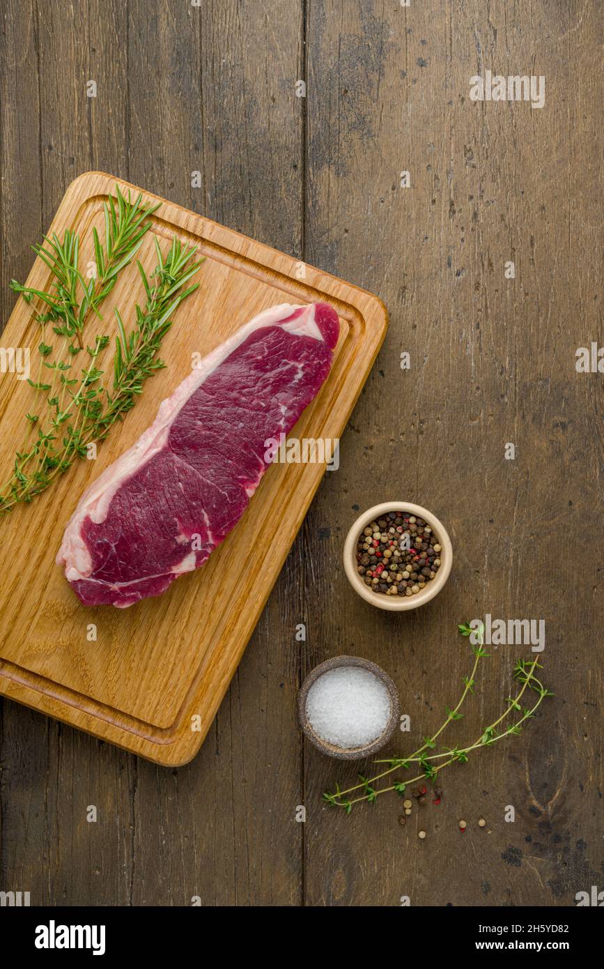 Raw striploin with thym, rosemary, salt and pepper on wooden cutting ...