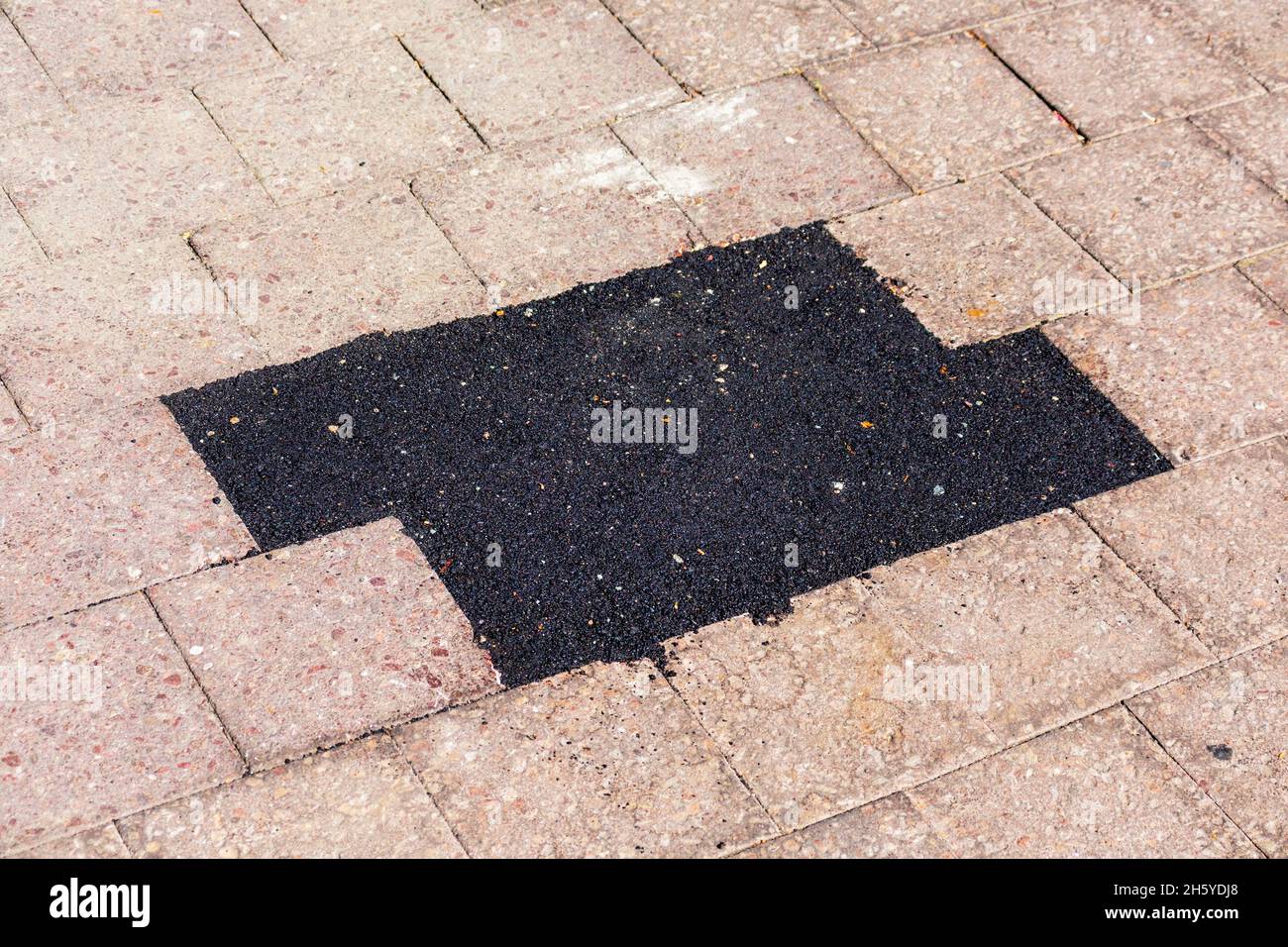 Fresh asphalt patch on red tile. Pedestrian walkway temporary repair ...
