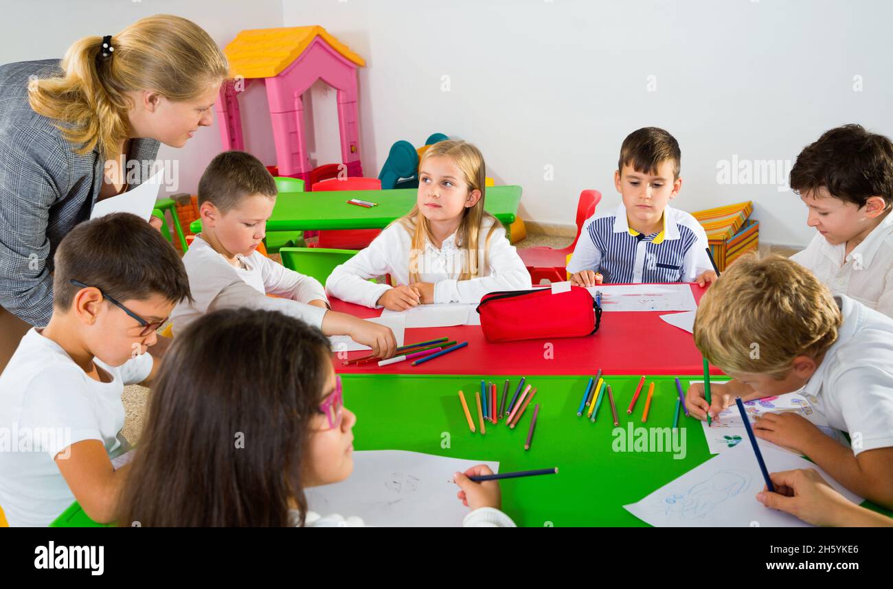 Female teacher helping schoolkids drawing with color pencils in ...
