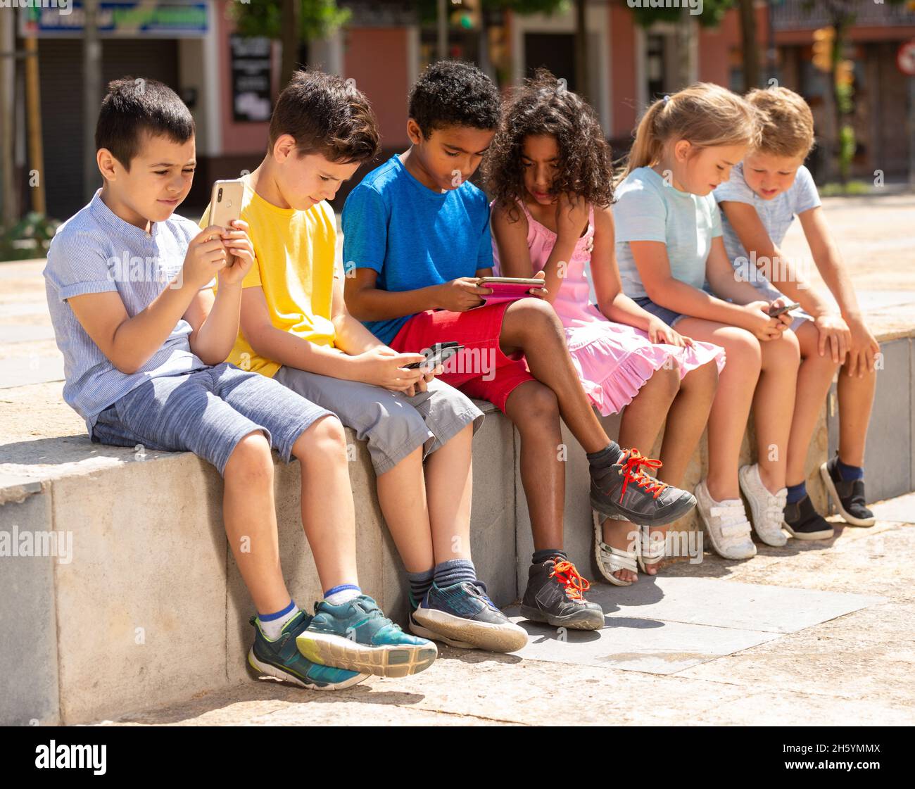 Positive children with mobile devices sitting at urban street Stock ...