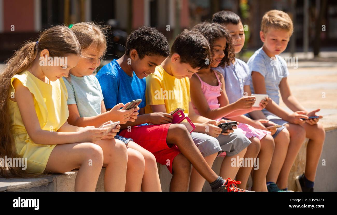 Children chatting on their smartphone, sitting on parapet Stock Photo ...