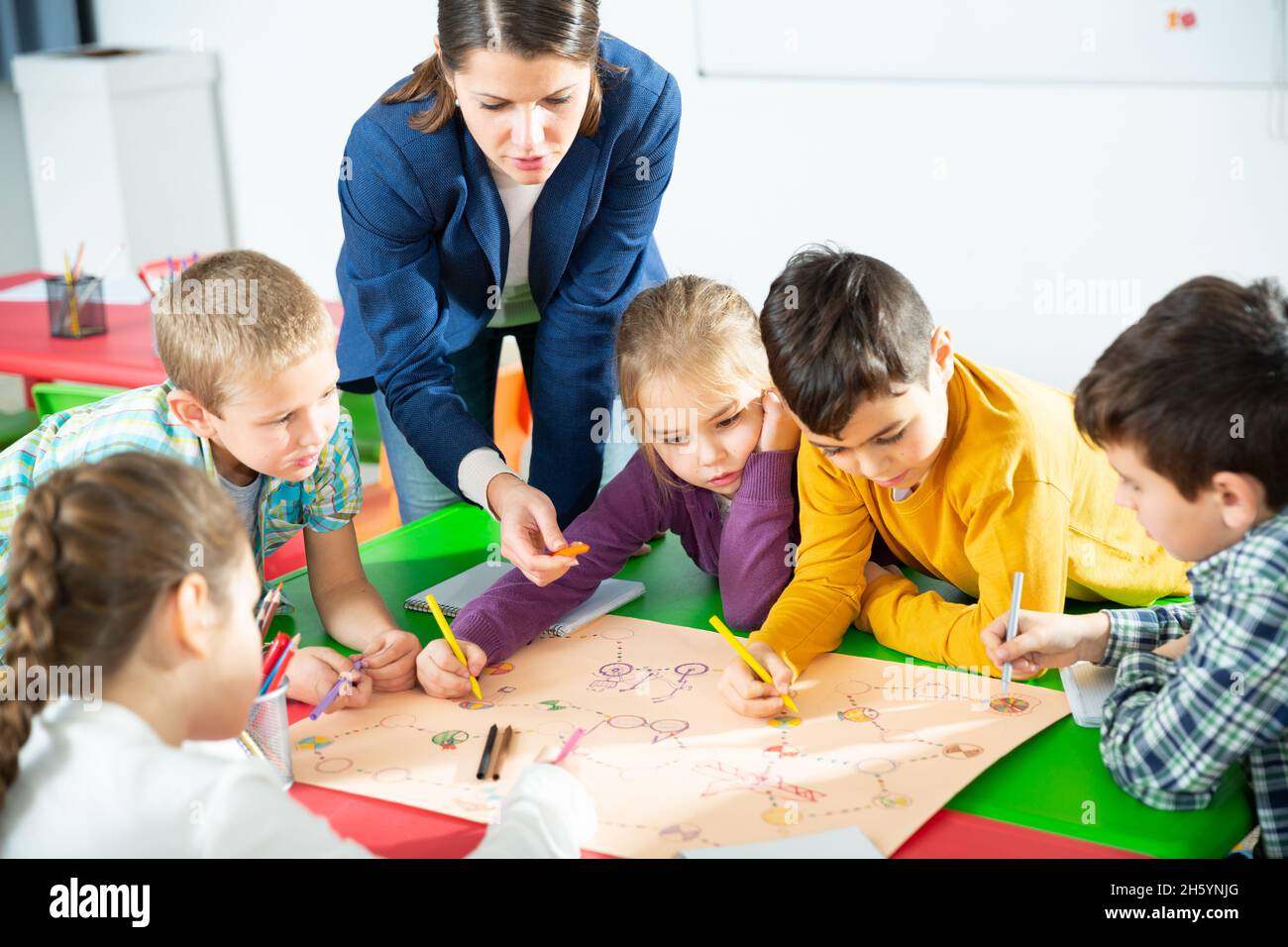 Teacher and collective of elementary age children draw together a board ...