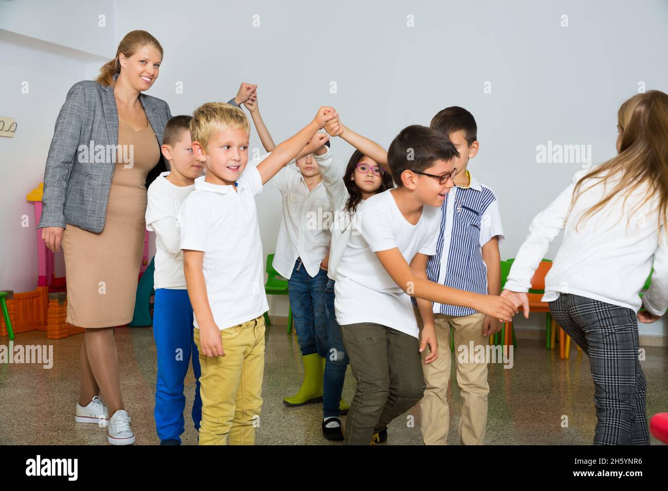 Kids playing thread and needle game with teacher Stock Photo - Alamy