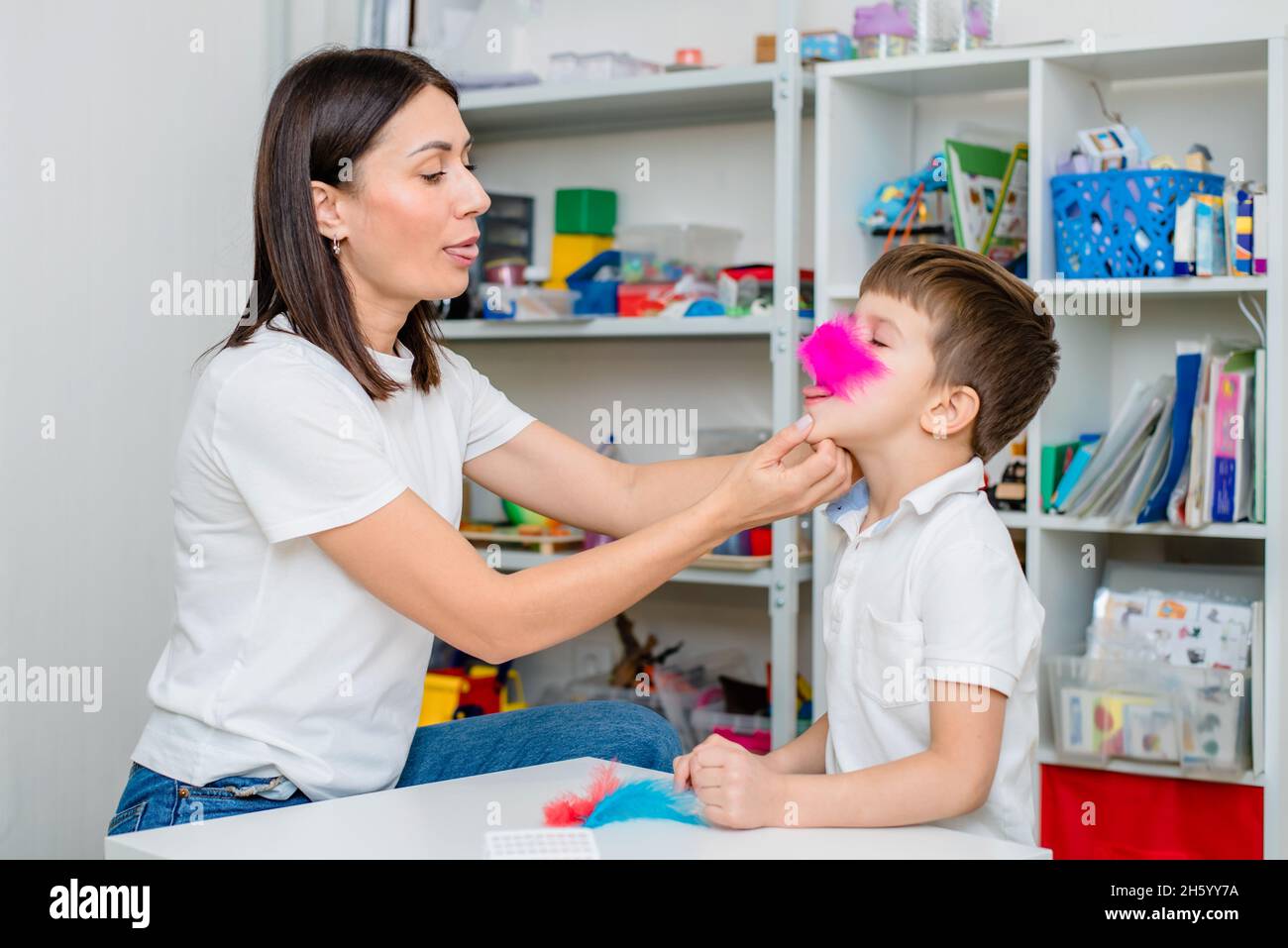 A woman speech therapist teaches a child to blow correctly on colored ...