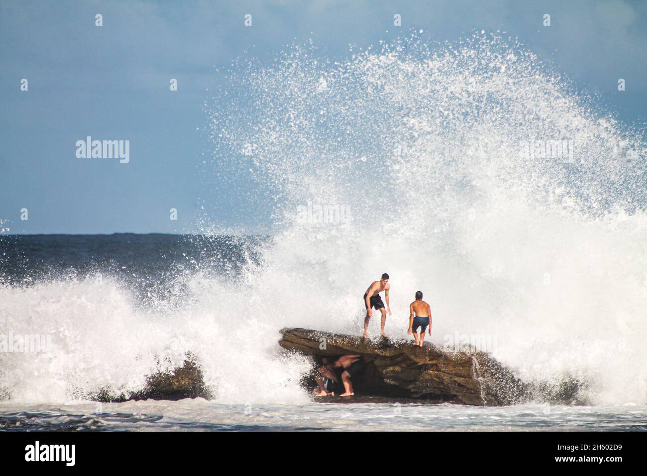 Swimmers on a rock at a beach during a wave splash Stock Photo - Alamy