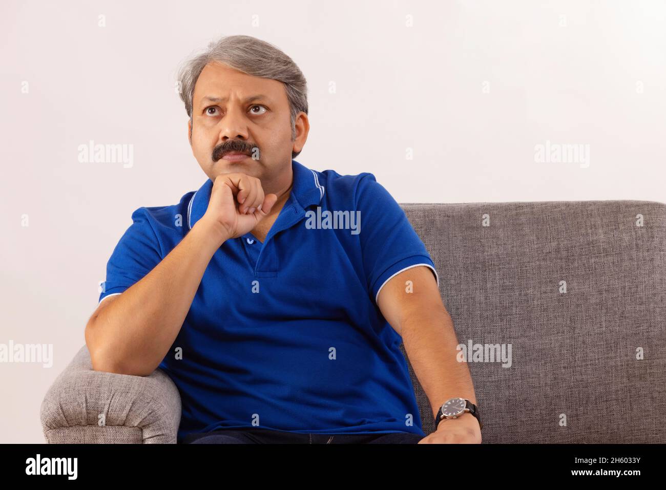 Man thinking seriously while sitting on sofa Stock Photo - Alamy
