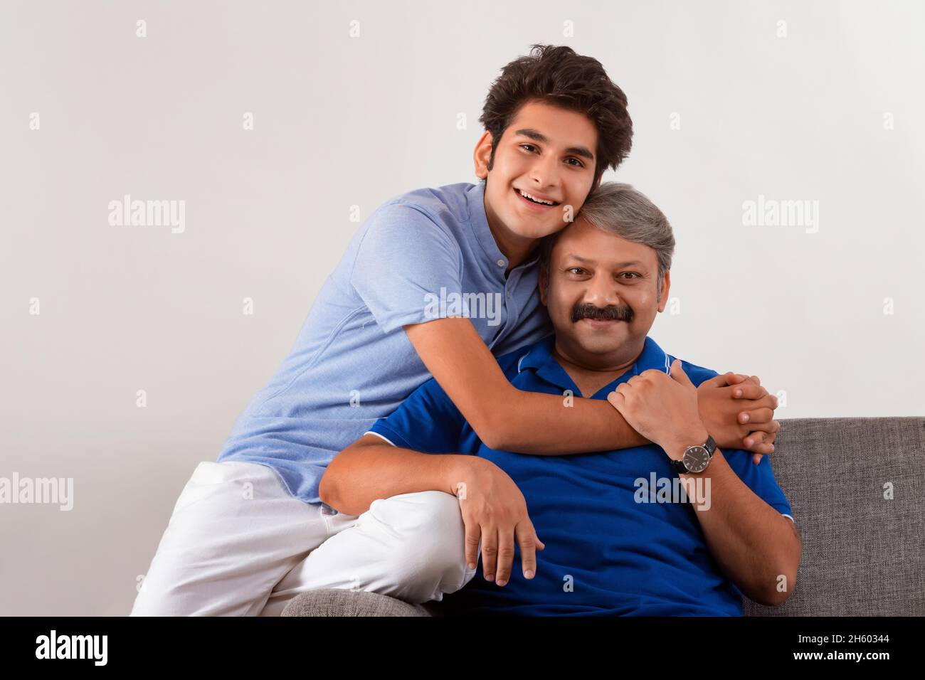 Young boy hugging his father while sitting on sofa Stock Photo - Alamy