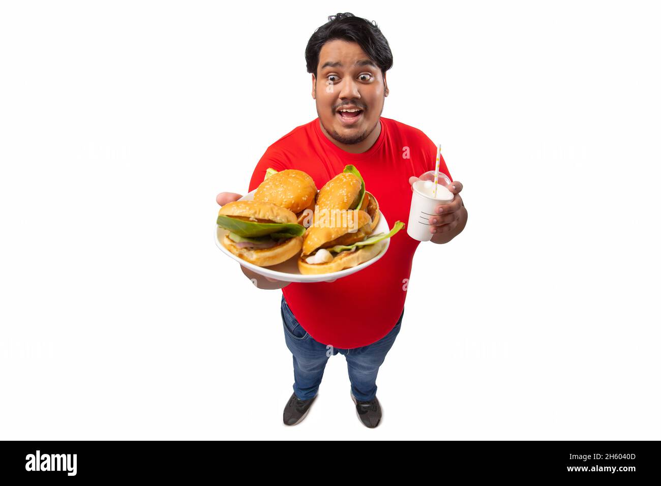 Portrait of a fat man holding a drink greedily devouring at plate of ...