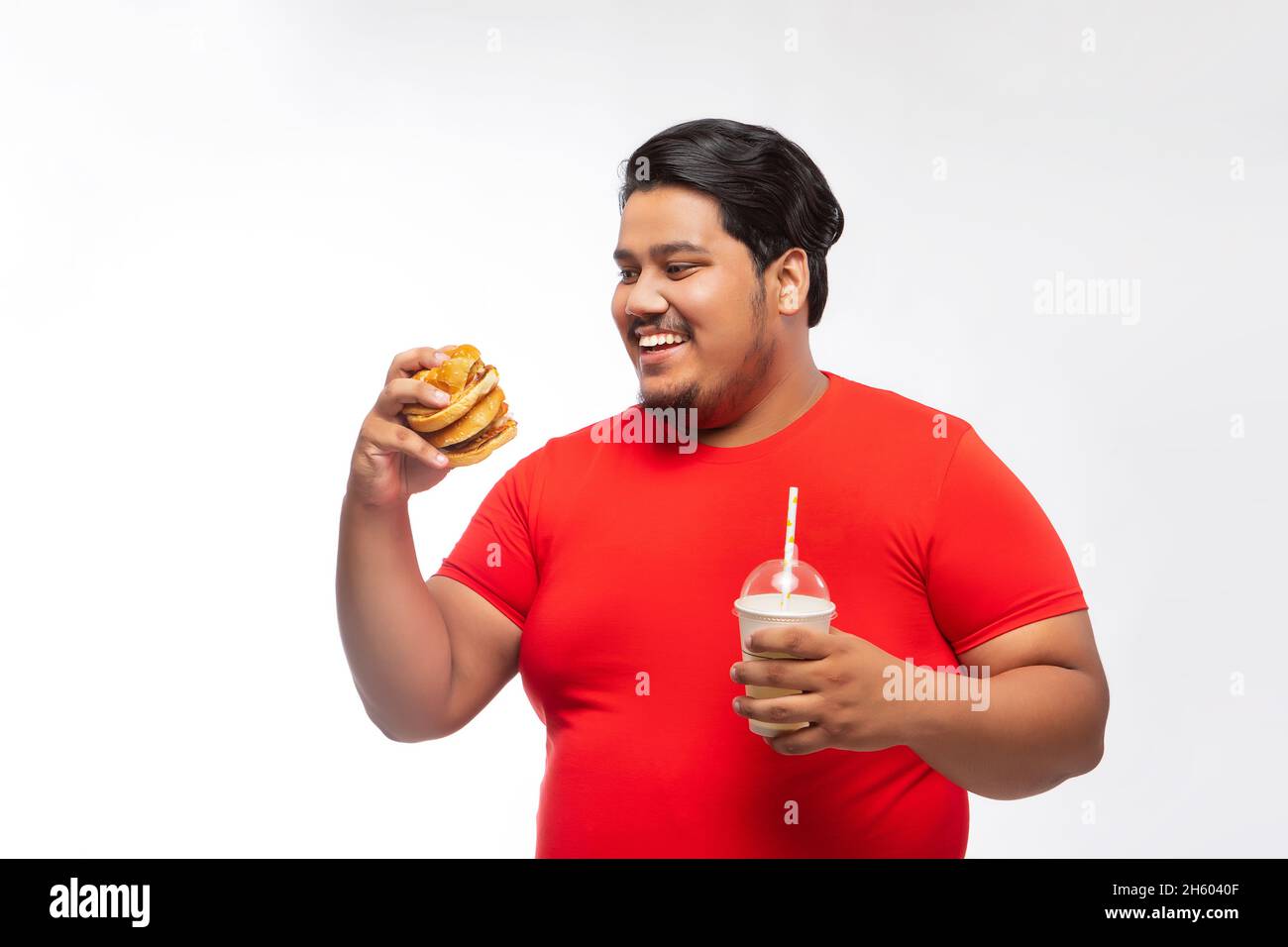 Portrait of a fat man holding a drink greedily devouring at burger ...