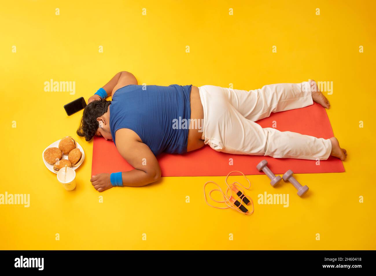 A fat man sleeping on yoga mat amidst dumbles,skipping rope,Burger ...