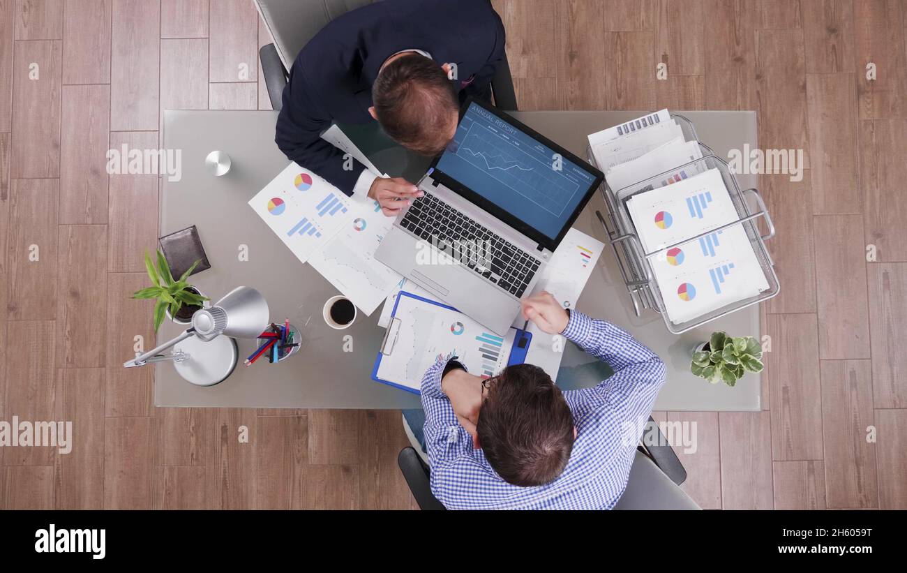 Top view of businessmen analyzing management statistics using laptop ...