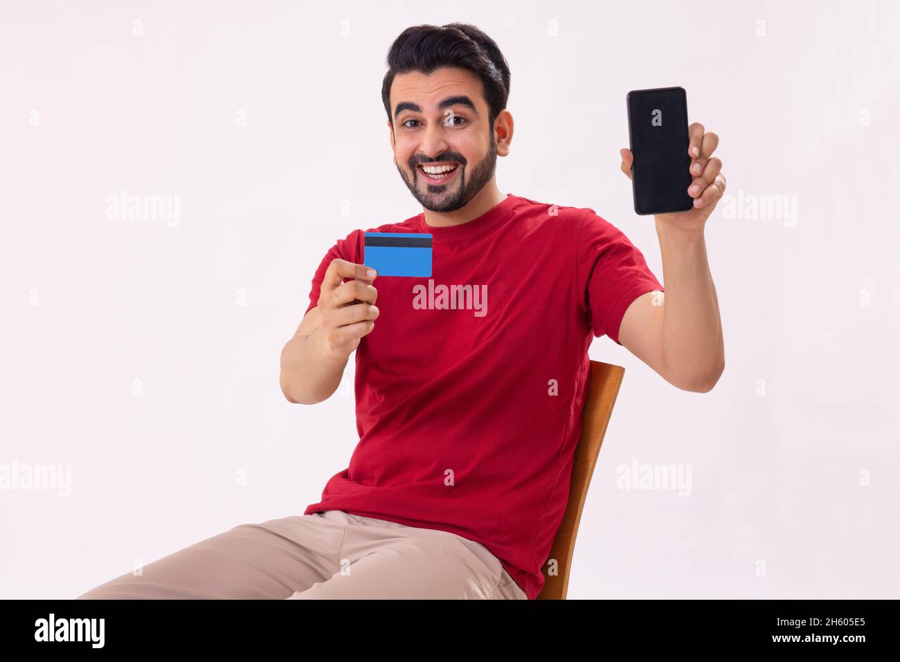 A MAN HAPPILY SHOWING MOBILE PHONE AND DEBIT CARD IN FRONT OF CAMERA ...
