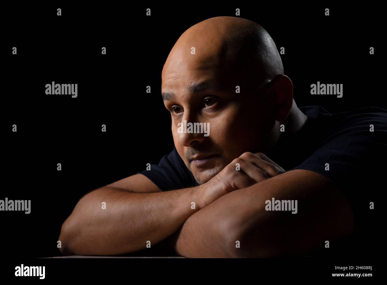 Portrait of a bald man gazing with an anxious look against dark black ...