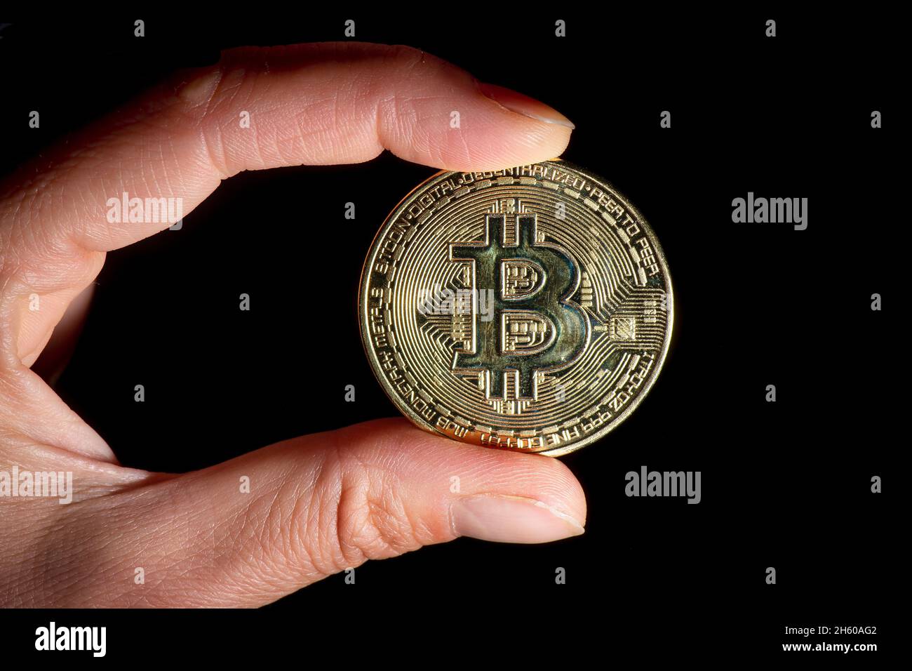 Bit Coin held between thumb and forefinger on black background Stock ...