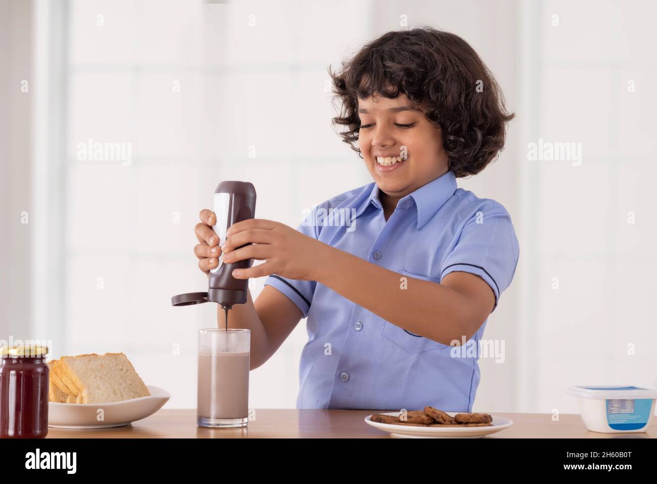 Young boy in school uniform pouring chocolate syrup into a glass of ...