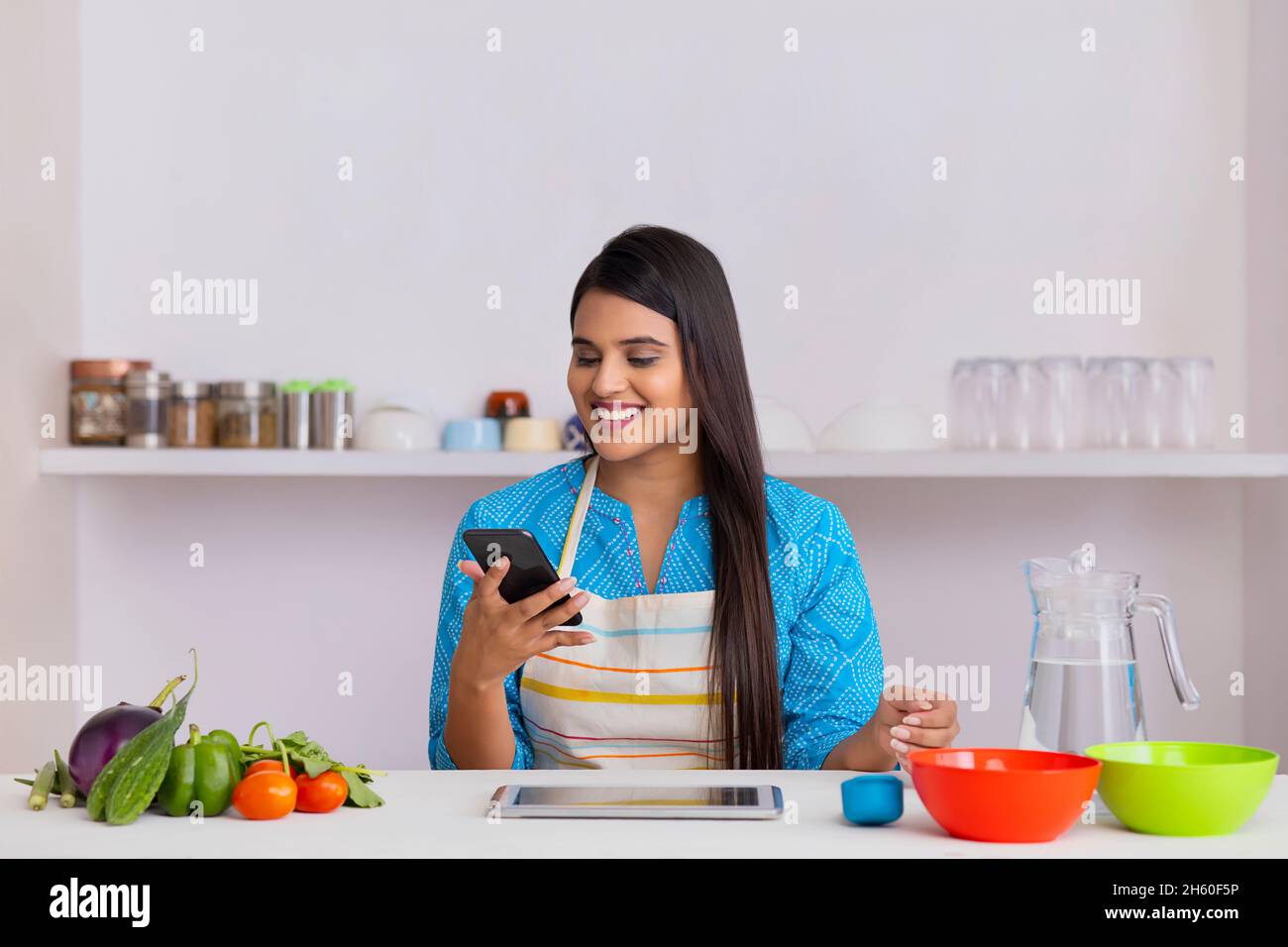 Indian woman watching smartphone while sitting in kitchen Stock Photo ...