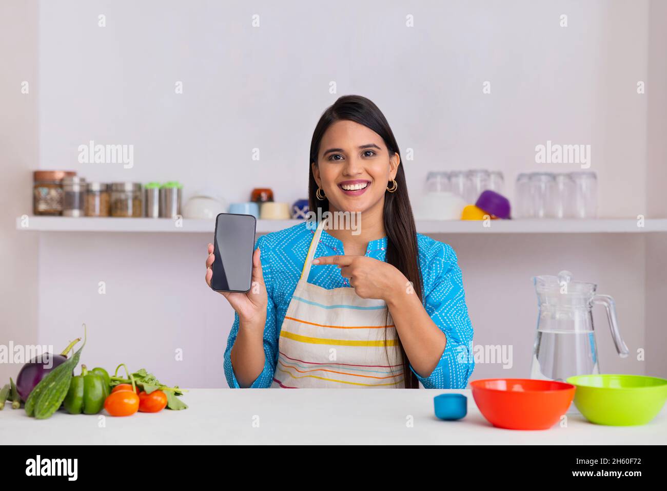 Indian woman showing her smartphone while sitting in kitchen Stock ...