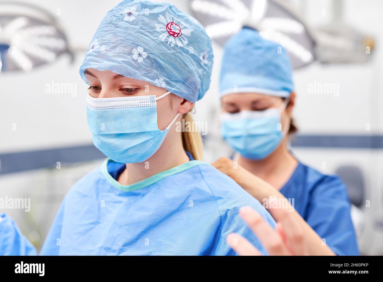 Surgical nurse helps female doctor put on protective clothing before an ...