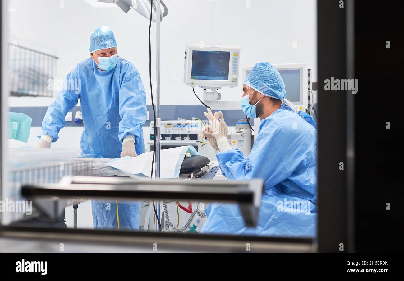 Two surgeons in protective clothing sit exhausted in the intensive care ...