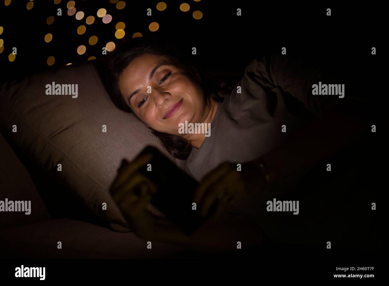 Indian woman watching smartphone at night while lying on bed Stock ...