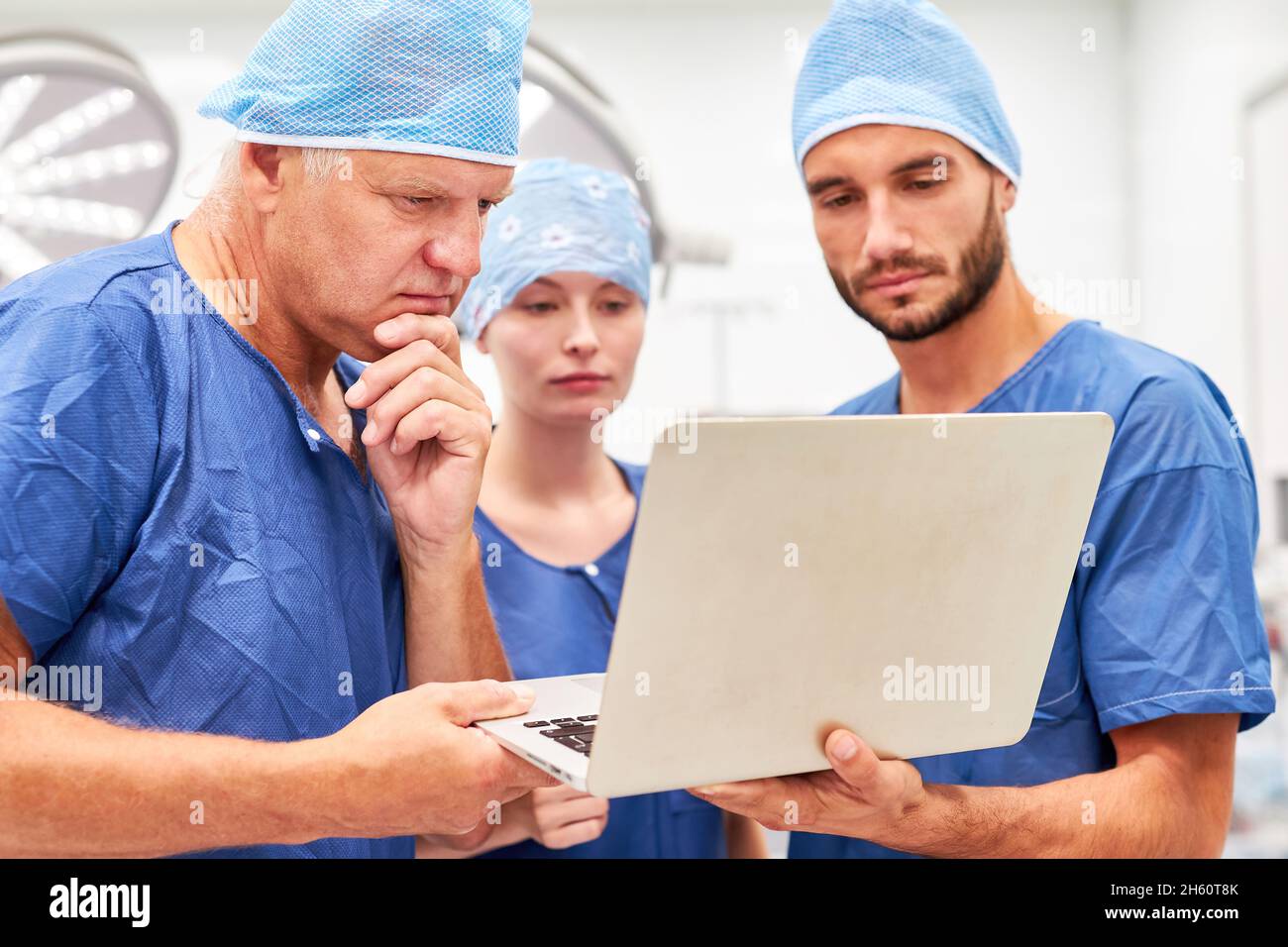 Doctors on surgery team look together on laptop computer before an ...