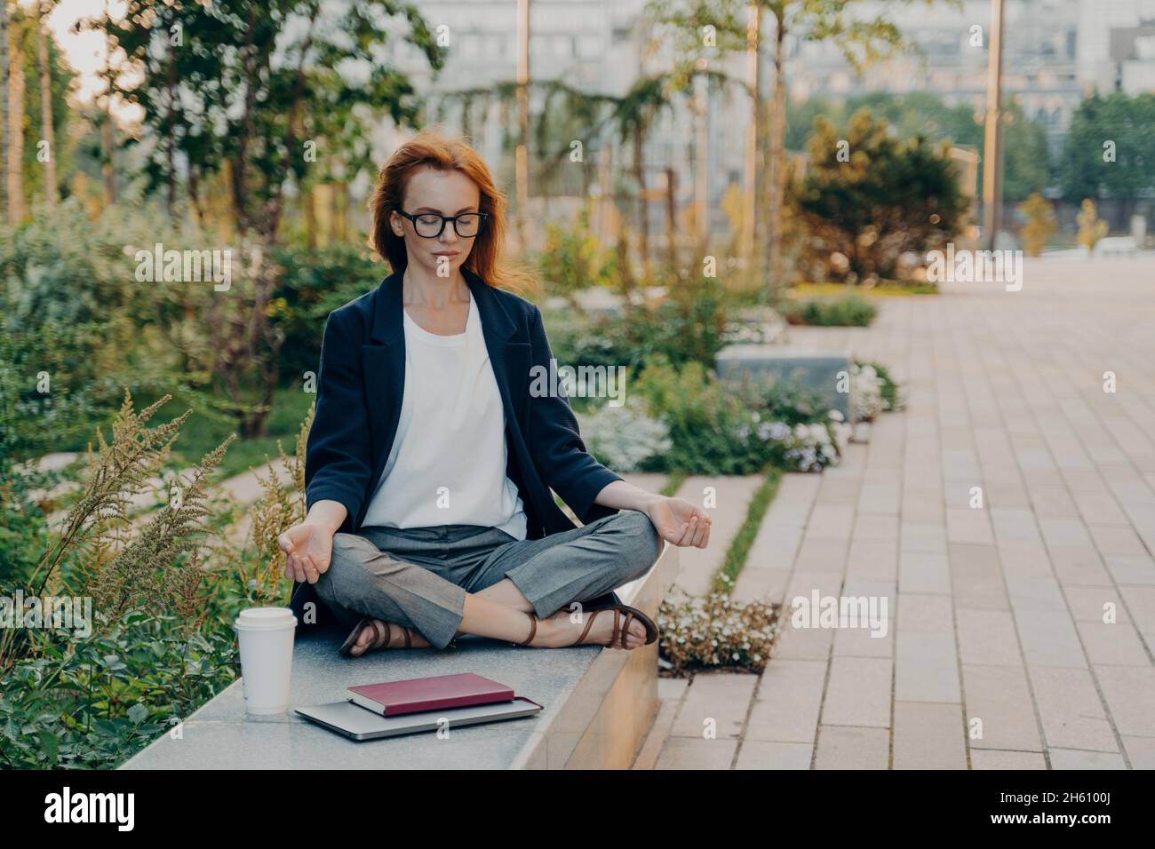 Young relaxed redhead woman meditates in park feels calm sits in lotus ...
