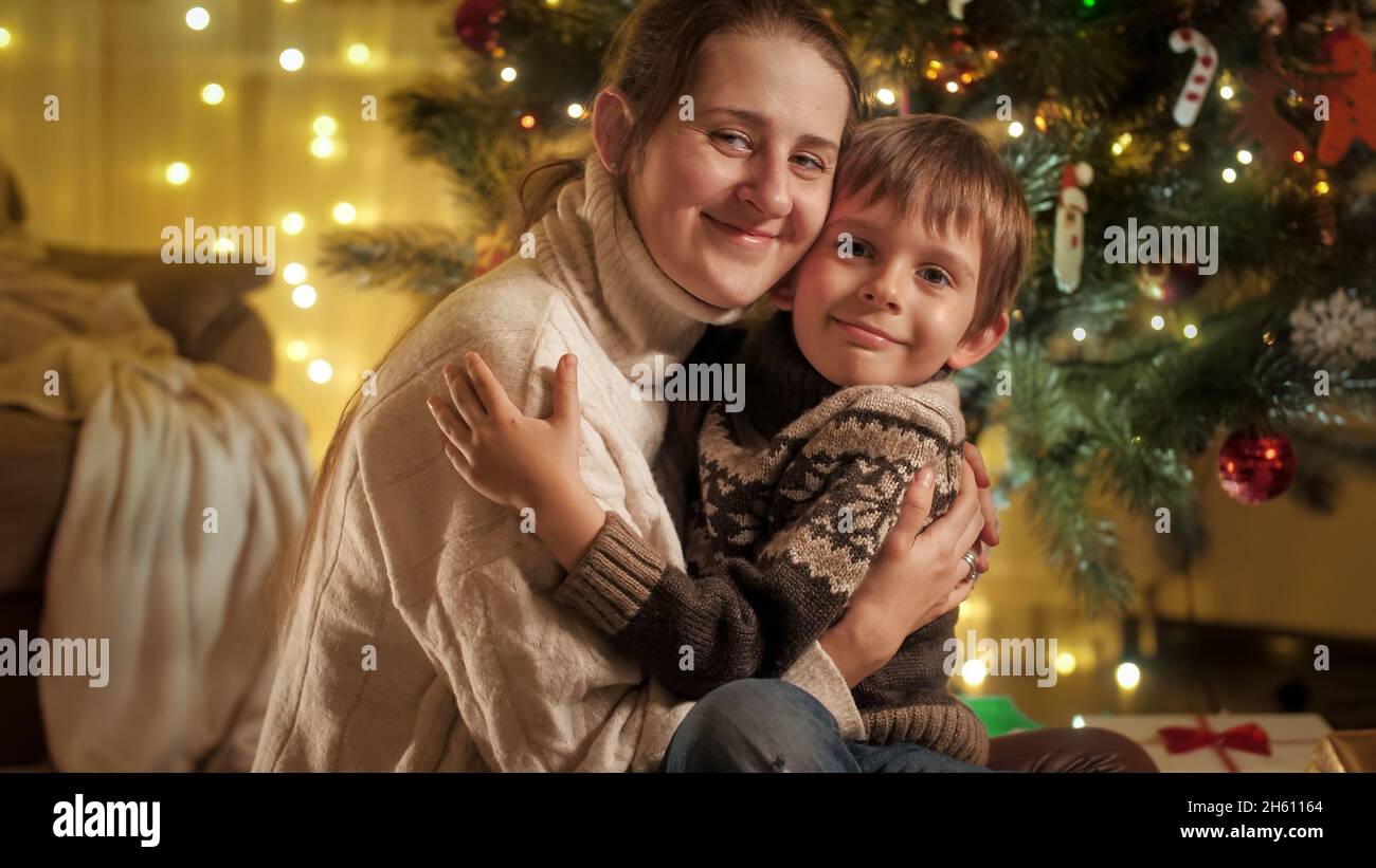 Portrait of cheerful smiling boy with mother hugging next to Christmas ...