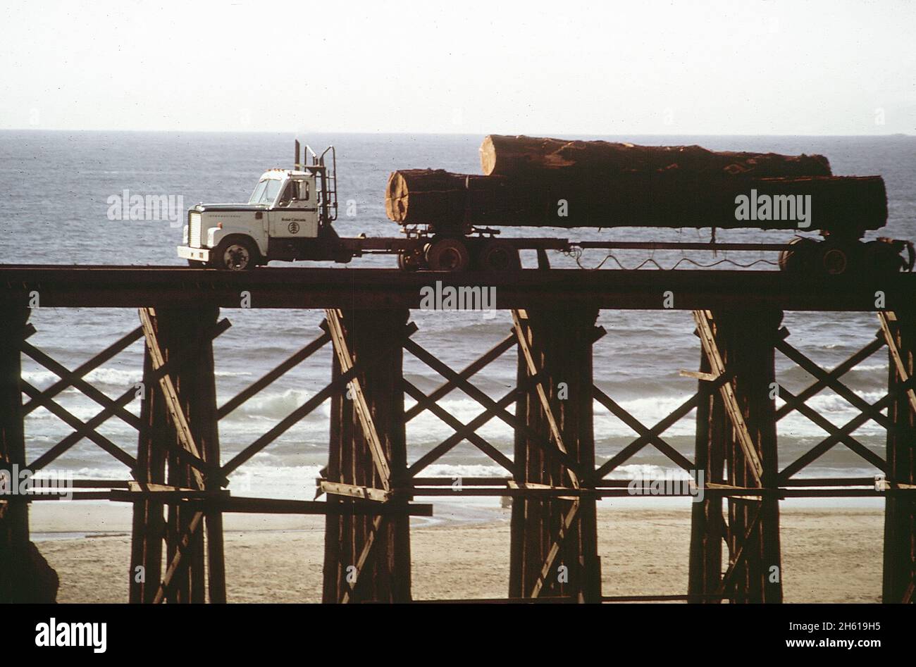 1970s America: Logging truck hauling large logs drives over a bridge in ...