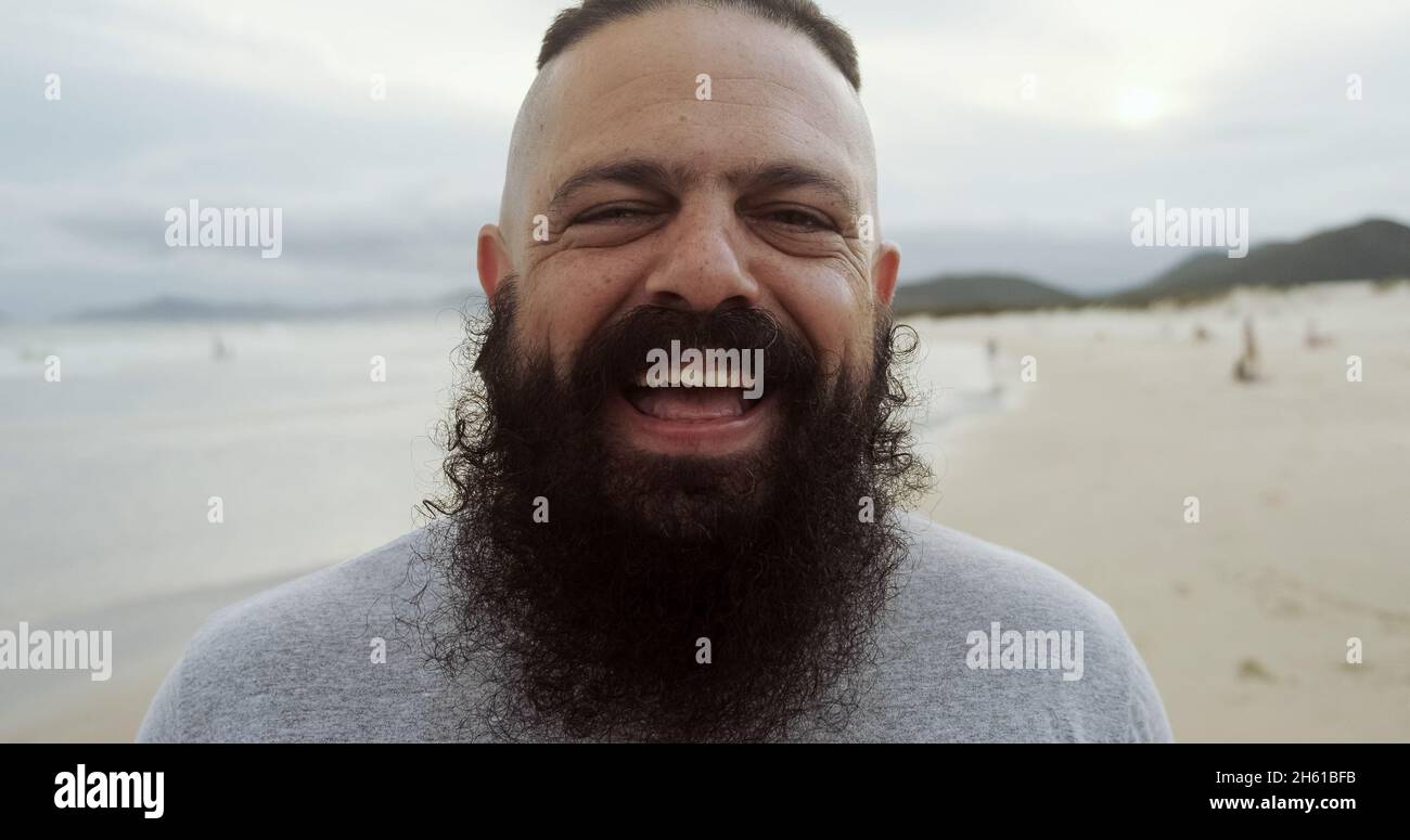 Happy latin man with big beard on a beach looking at camera and smiling ...
