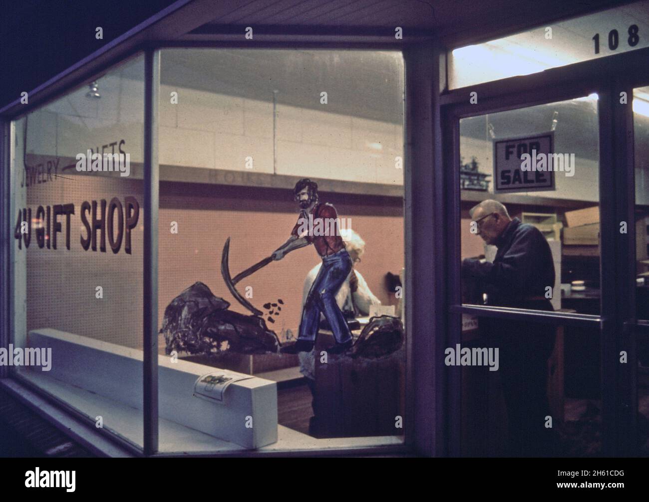 1970s America: Elderly man and woman seen through a gift shop window ca ...