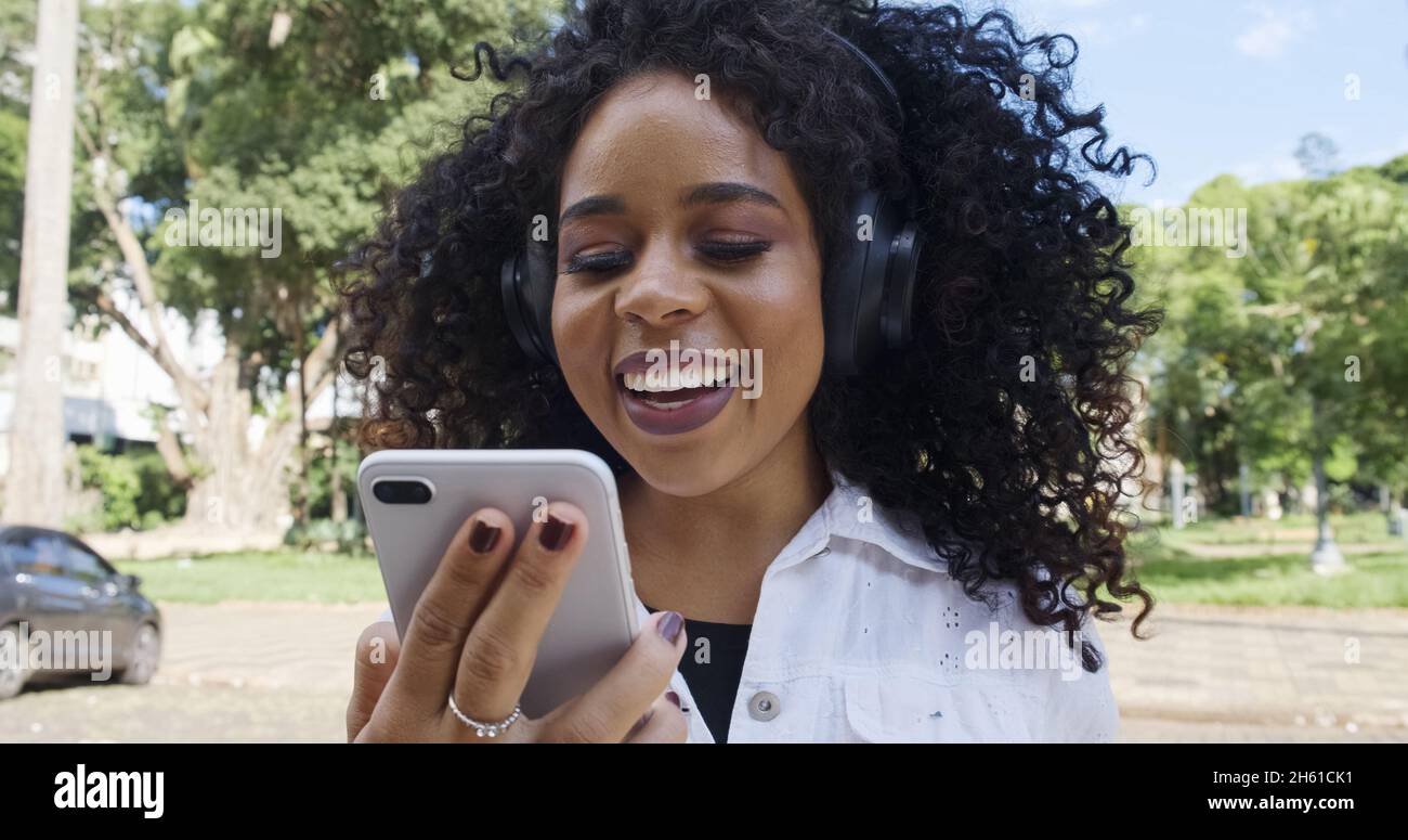Young curly hair black woman walking using cell phone. Texting on ...