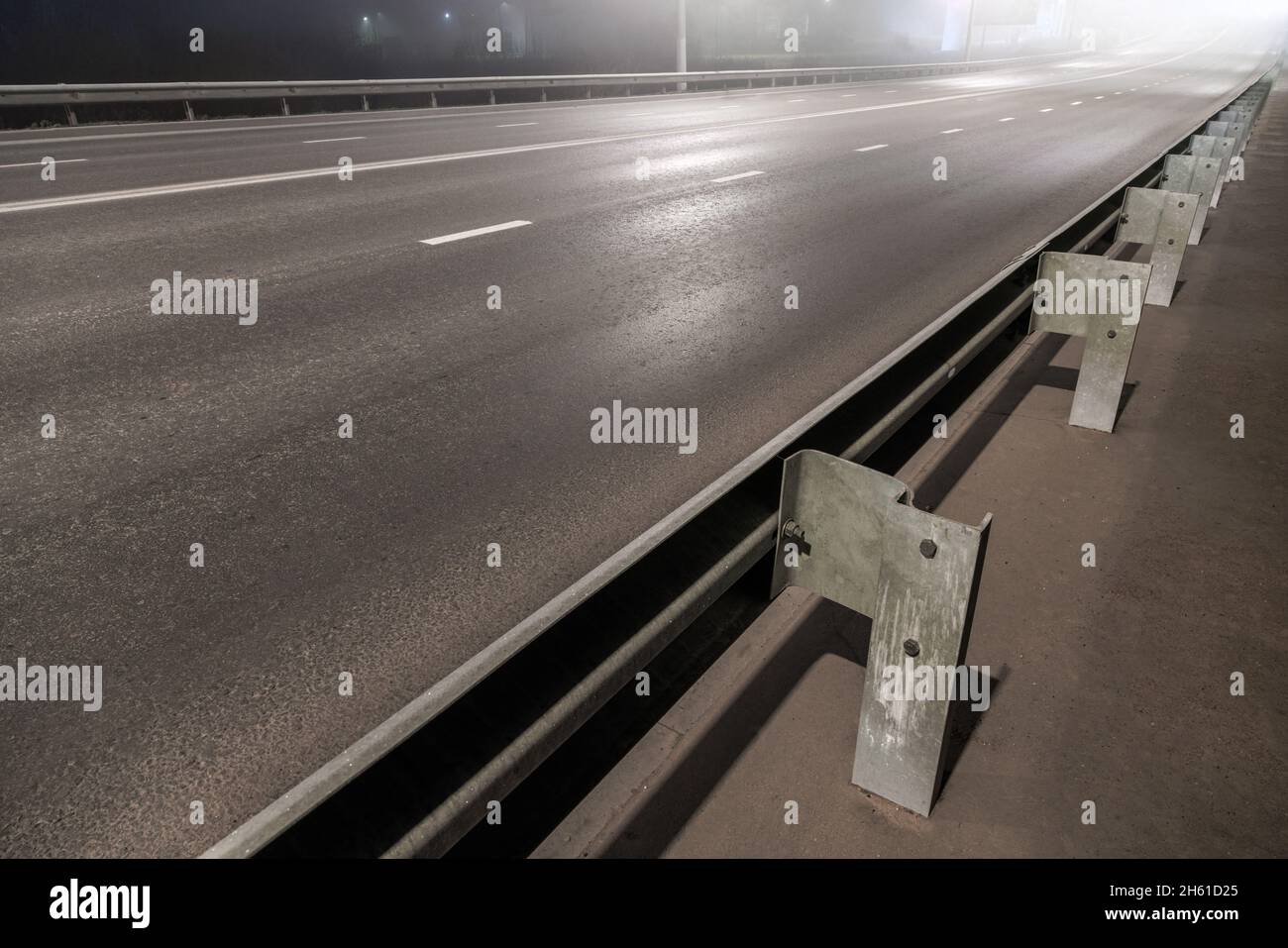 illuminated empty foggy night road with rigid guardrails, traffic ...