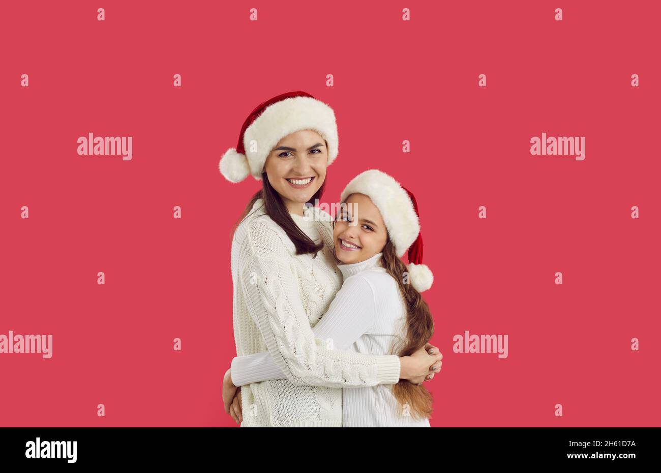Smiling mom and daughter in Santa hats on red background Stock Photo ...