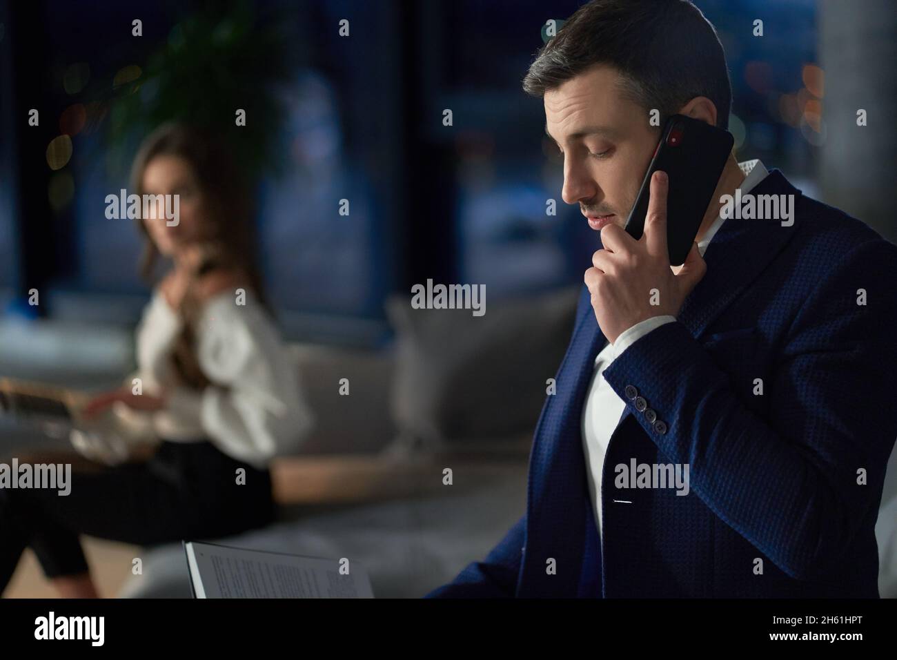 Focused caucasian businessman in suit having mobile conversation while his charming wife sitting ...