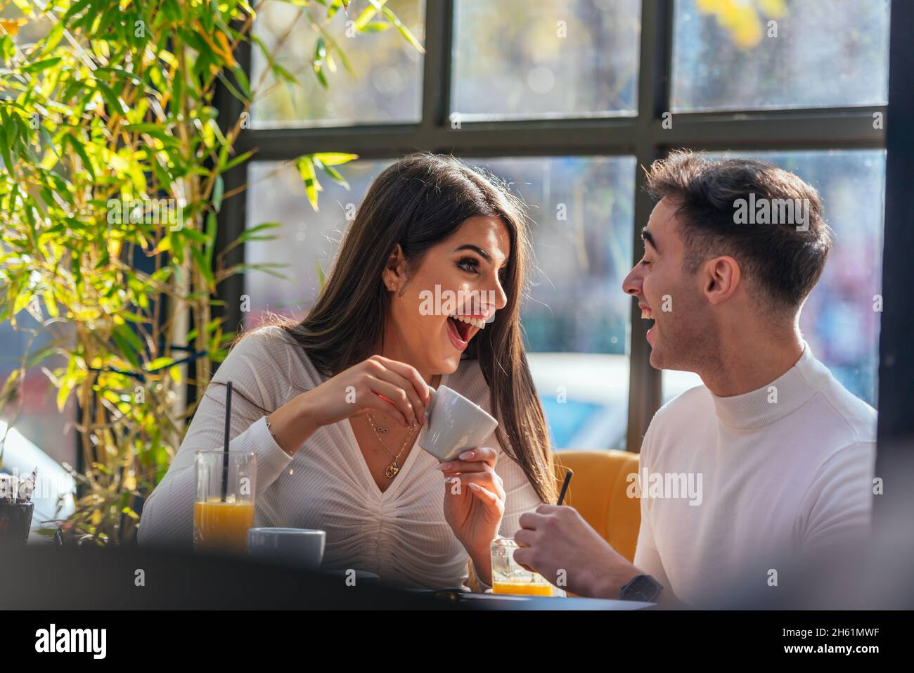 Two happy young people are laughing while sitting at a table in indoor ...