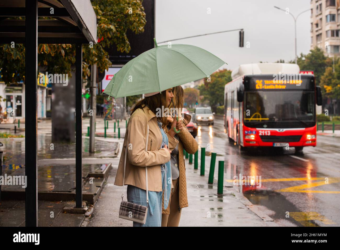 The Bus Is Arriving At The Bus Stop While The Two Girls Are Waiting For