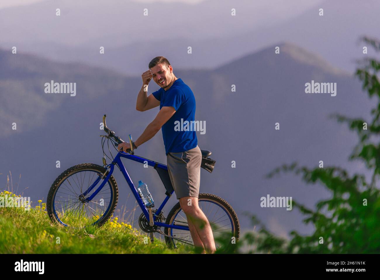 Tired cyclist is wiping his sweat off his face while pushing his ...