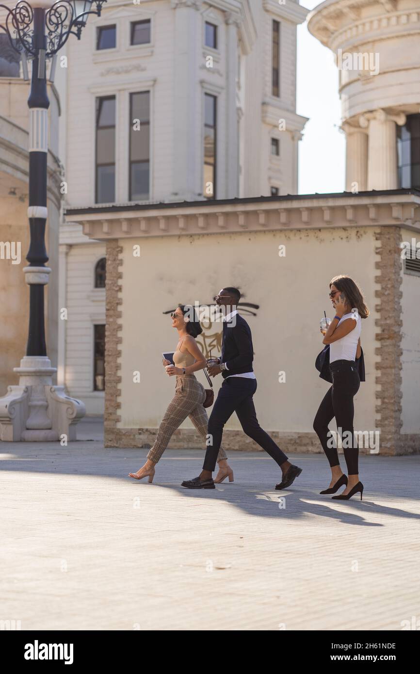 Three multiracial business people are smiling while walking fast ...