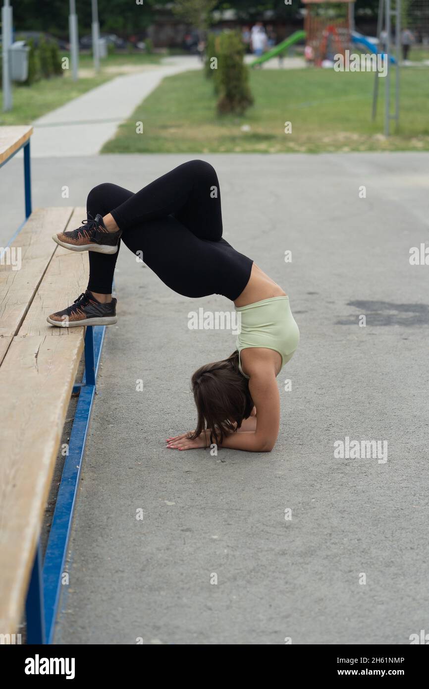 Adorable and attractive girl is bending so much on the wooden bench ...